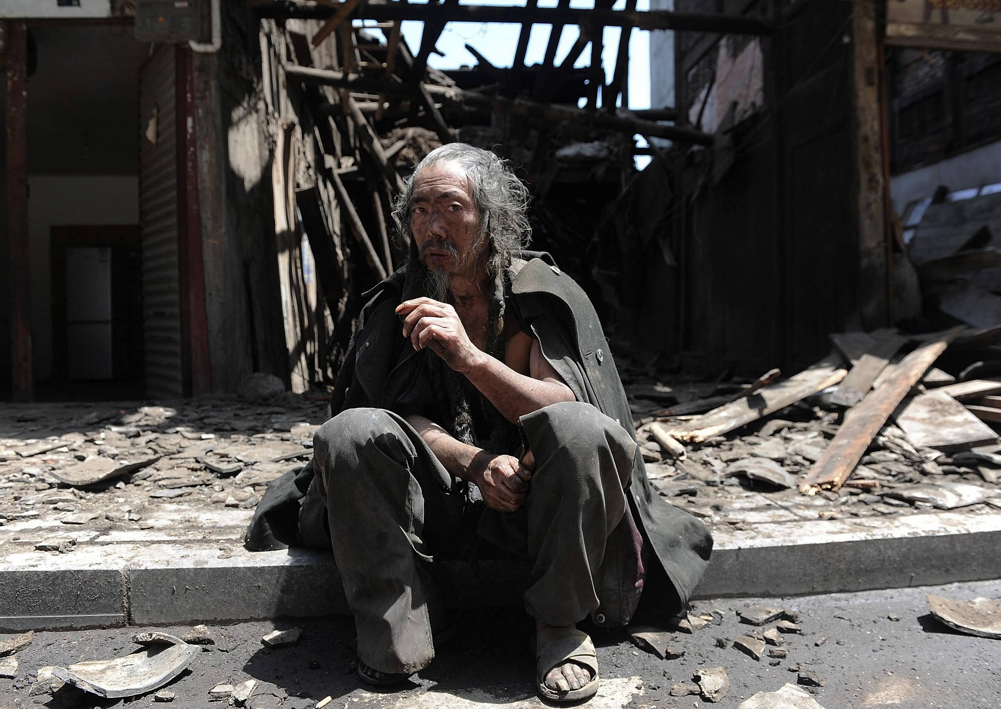 A man sits in front of houses destroyed by an earthquake in Sichuan ...